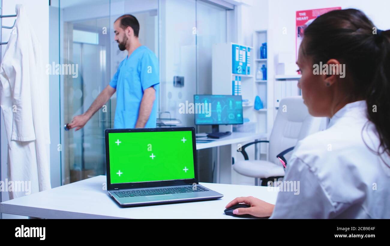 Medical worker in white coat using laptop with green screen in hospital ...
