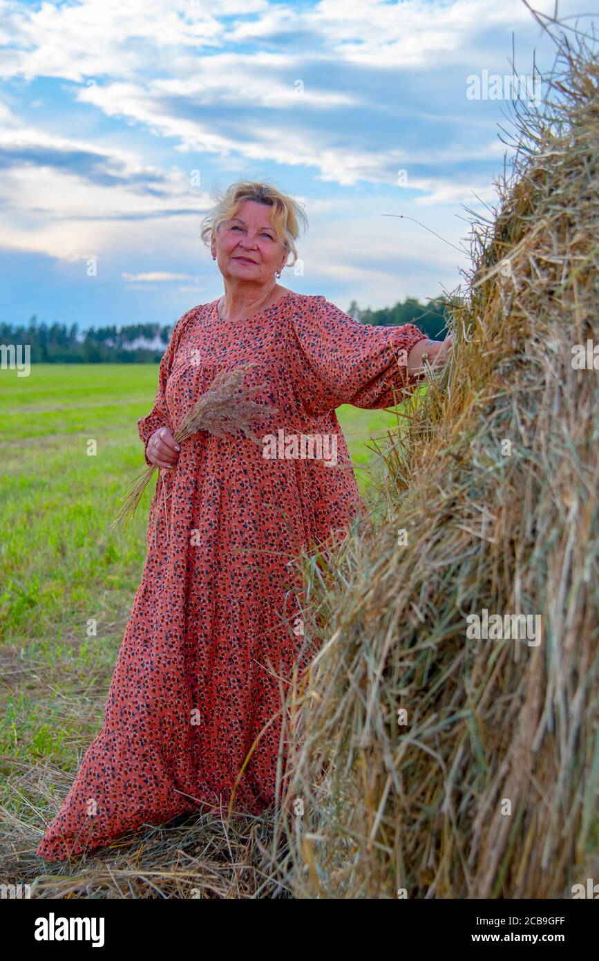 An elderly woman in a long country dress poses in haystacks Stock Photo ...