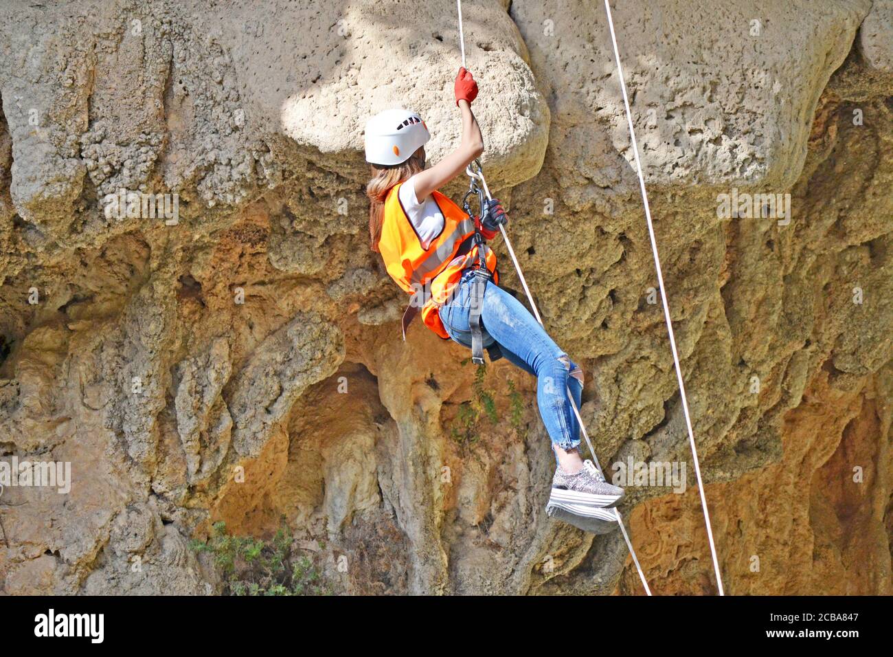 An active adventurer young lady going down the rocks using safety ropes ...