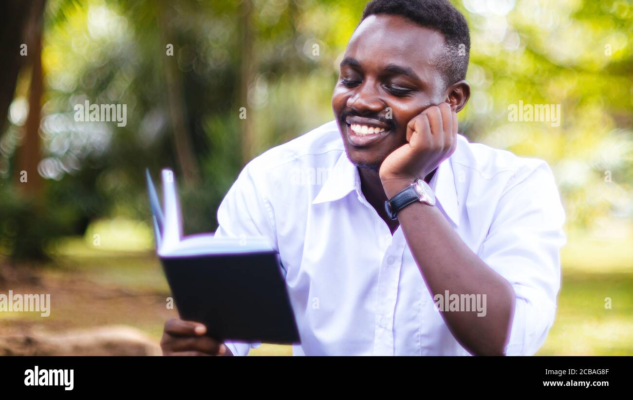 Portrait happy smiling african man reading book and wearing white shirt ...
