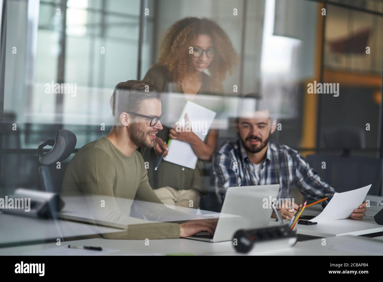 Helping coworkers. Three young happy colleagues using laptop and ...