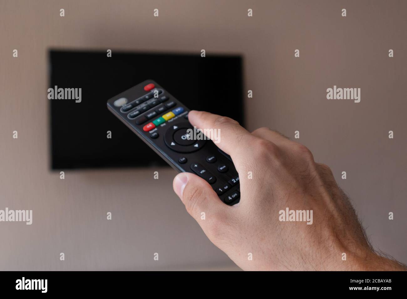 Male hand with tv remote control and blurred television with a black ...
