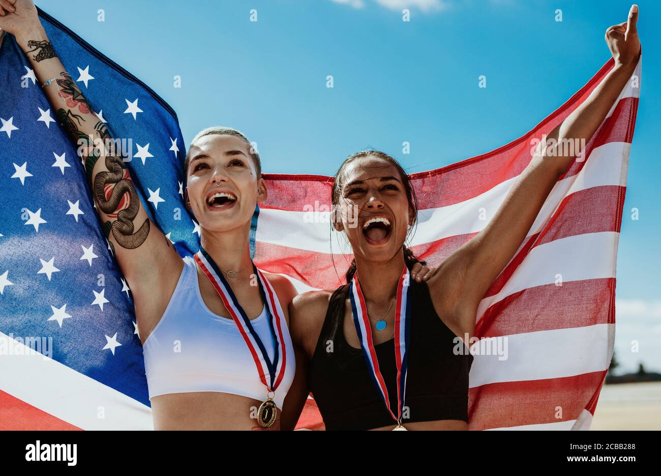 Female athletes celebrating victory holding american flag outdoors at ...