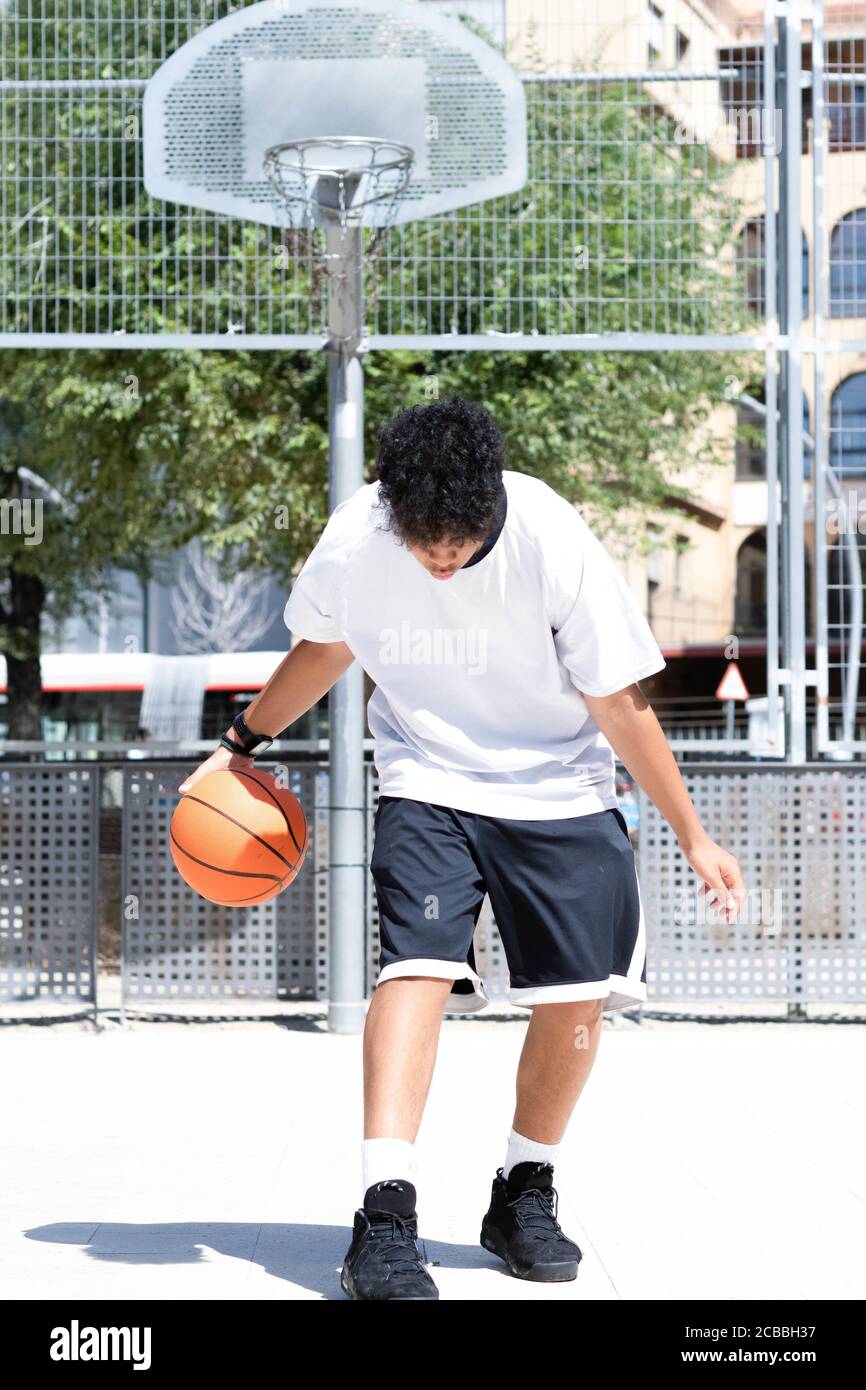 Vertical photo of afro teenage boy throwing the ball to the basket on ...
