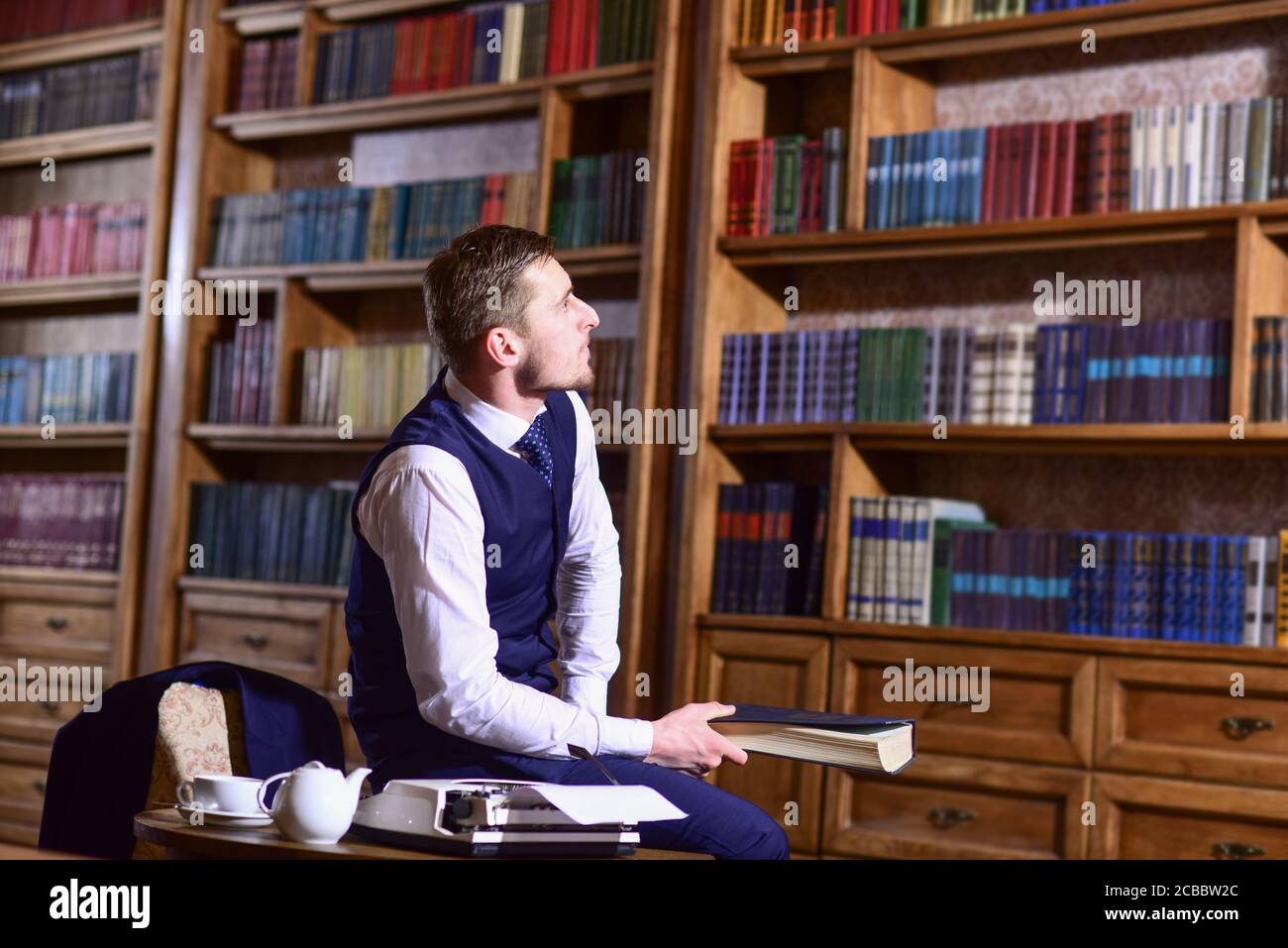 Professor with thoughtful face holds book in antique interior or old ...
