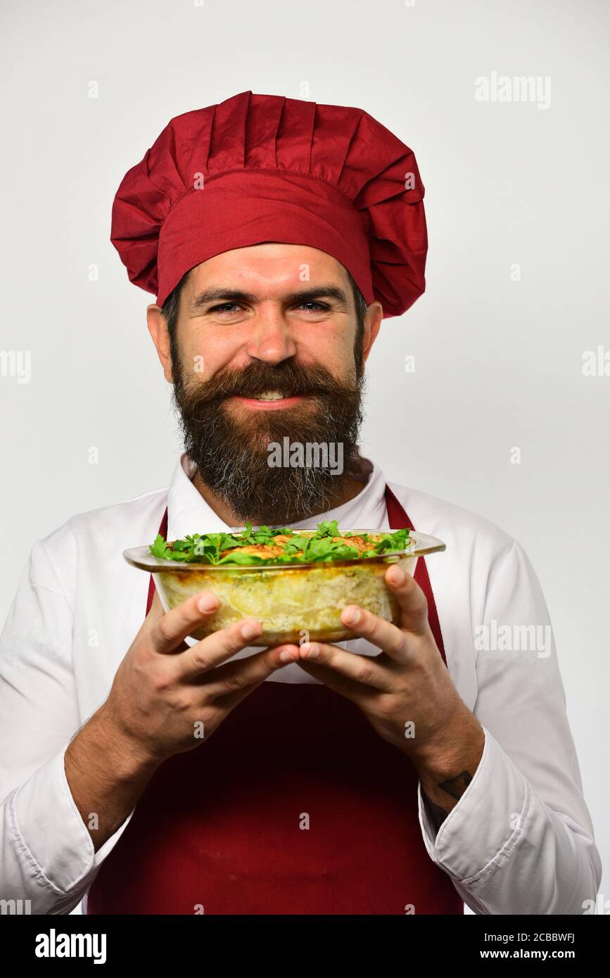 Cook with smile in burgundy uniform holds baked dish. Healthy nutrition ...