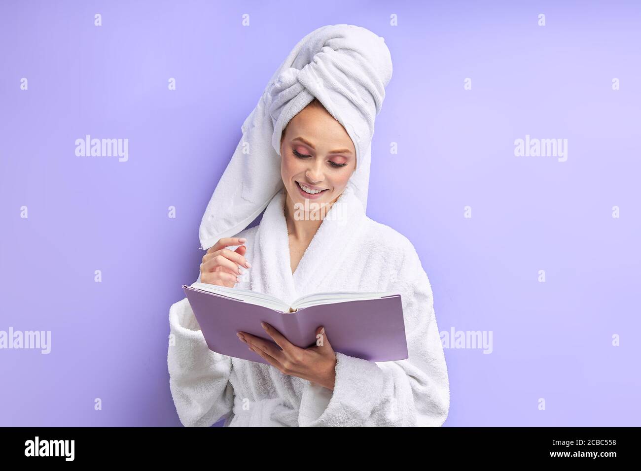 Caucasian woman wearing bathrobe and towel after shower reading book ...