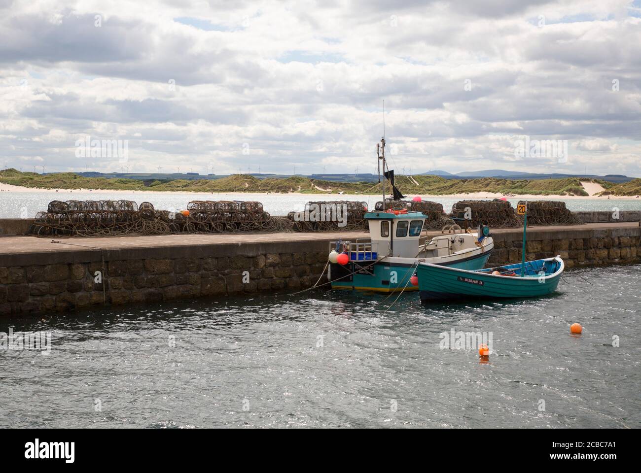 Boats in harbour with lobster pots stacked on pier wall, Beadnell Bay ...