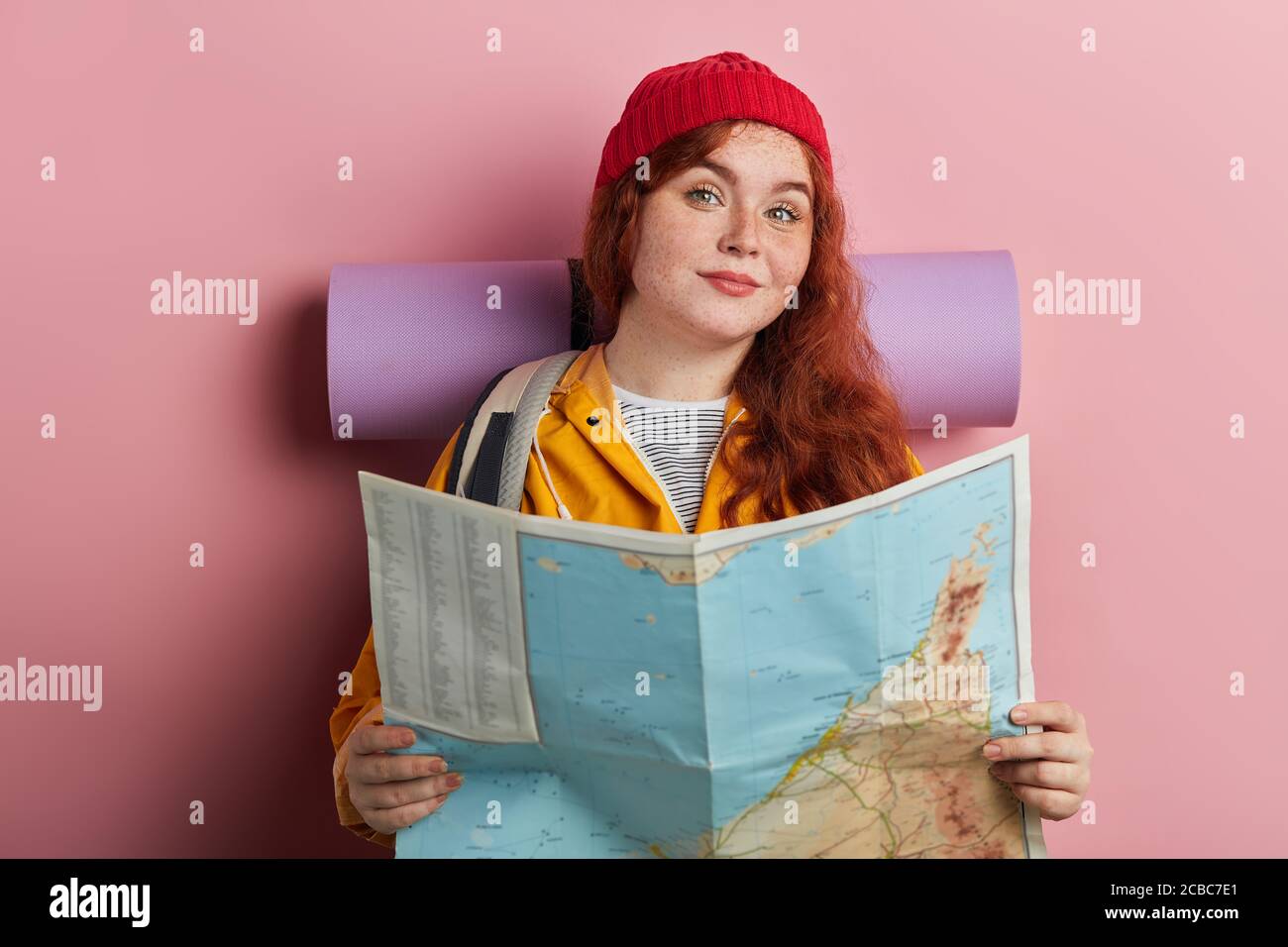 smiling positive ginger tourist holding a map, making decision where to ...