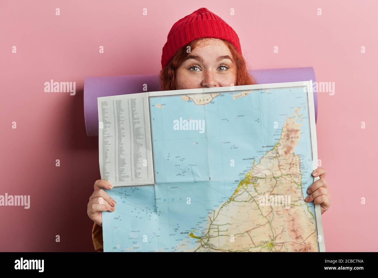 funny tourist hiding behind the map, close up portrait, isolated pink ...
