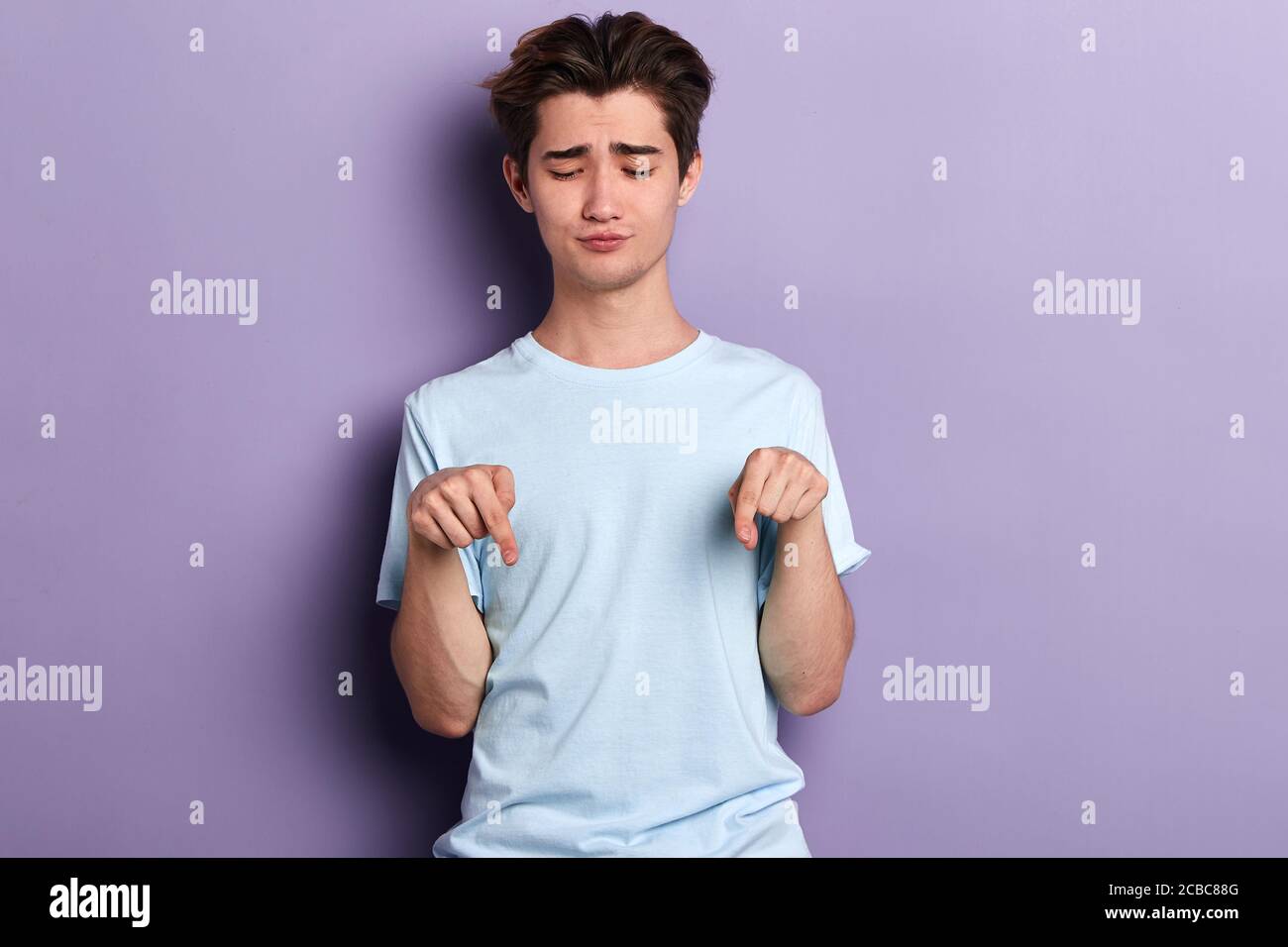 Handsome young poor unhappy depressed man pointing down, isolated on ...