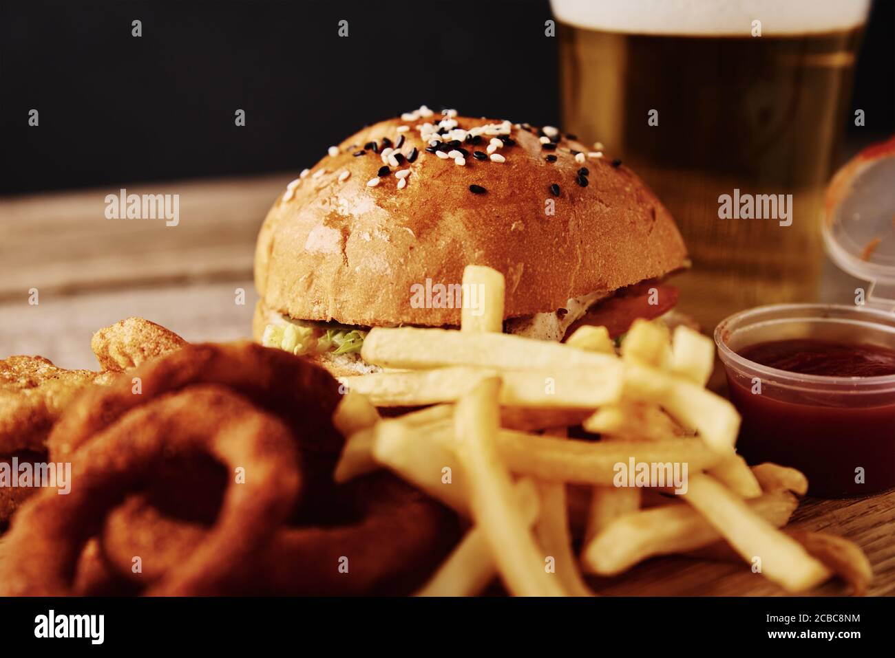 Different types of fastfood and snacks and glass of beer on table ...