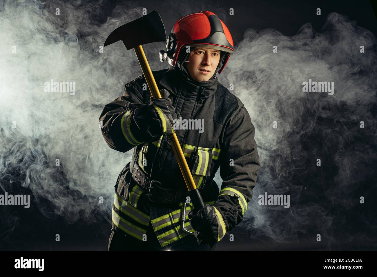 portrait of young caucasian fireman with hammer, wearing helmet and ...