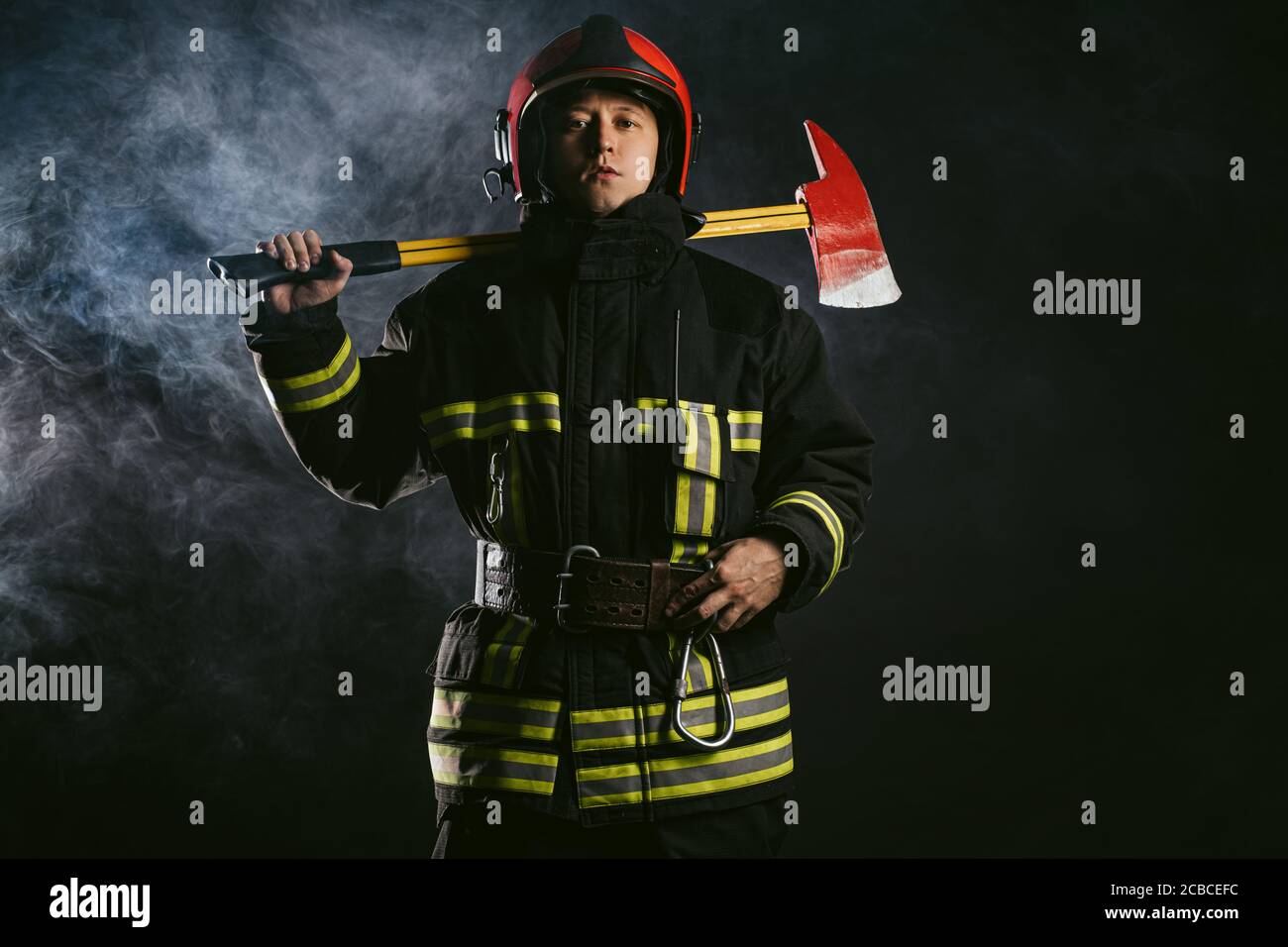 portrait of professional and confident fireman holding hammer, wearing ...