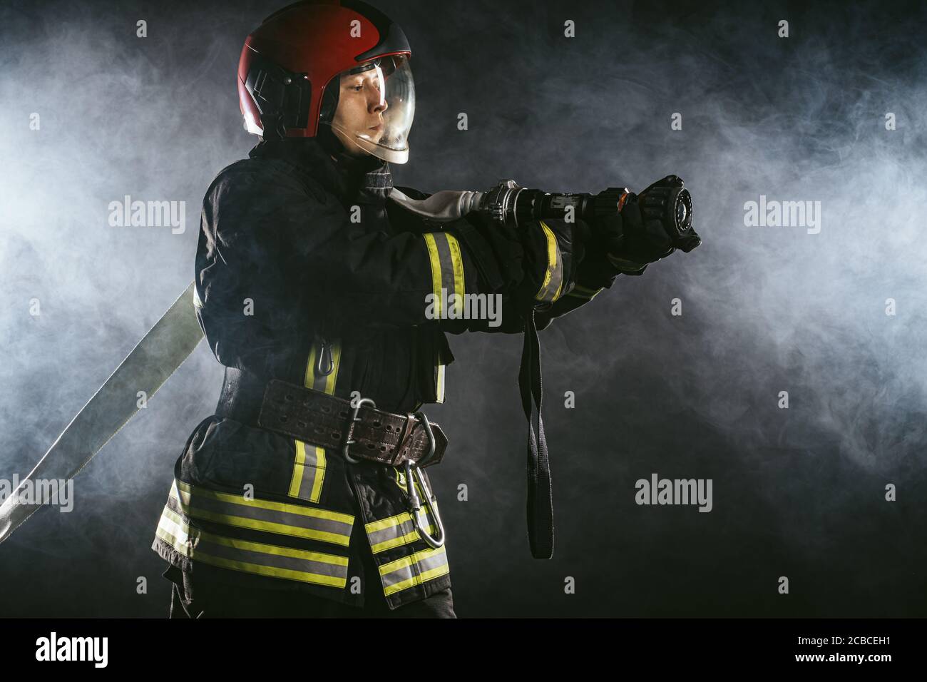 handsome fireman in helmet stand isolated in smoky space, wearing ...