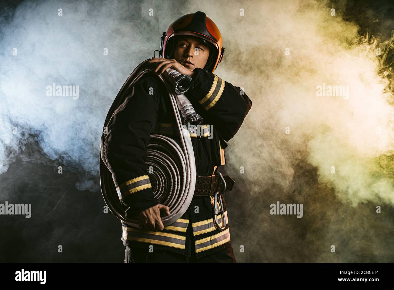 handsome fireman in helmet stand isolated in smoky space, wearing ...