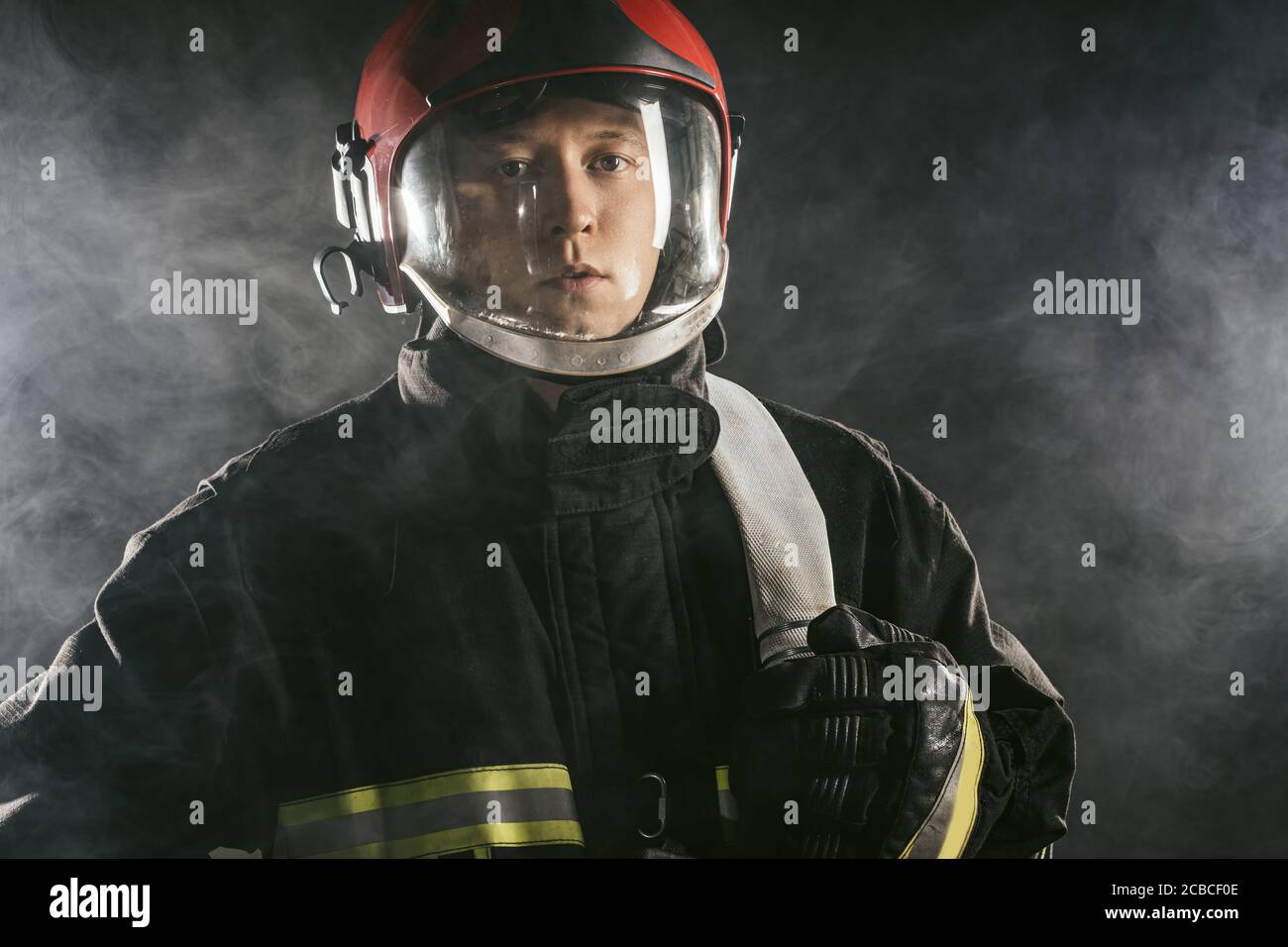 handsome fireman in helmet stand isolated in smoky space, wearing ...
