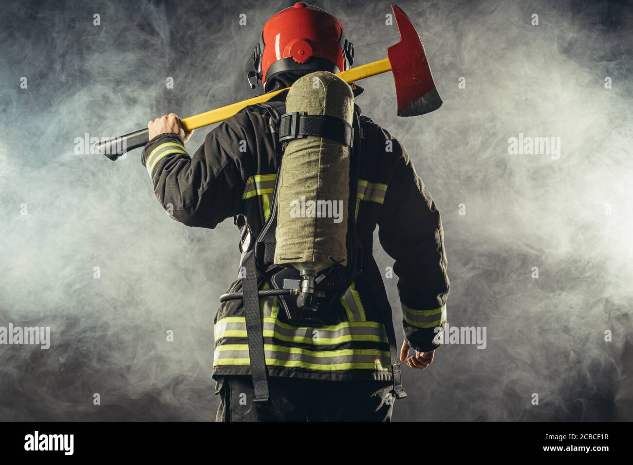 rear view on fire fighter stand holding hammer isolated over smoky ...