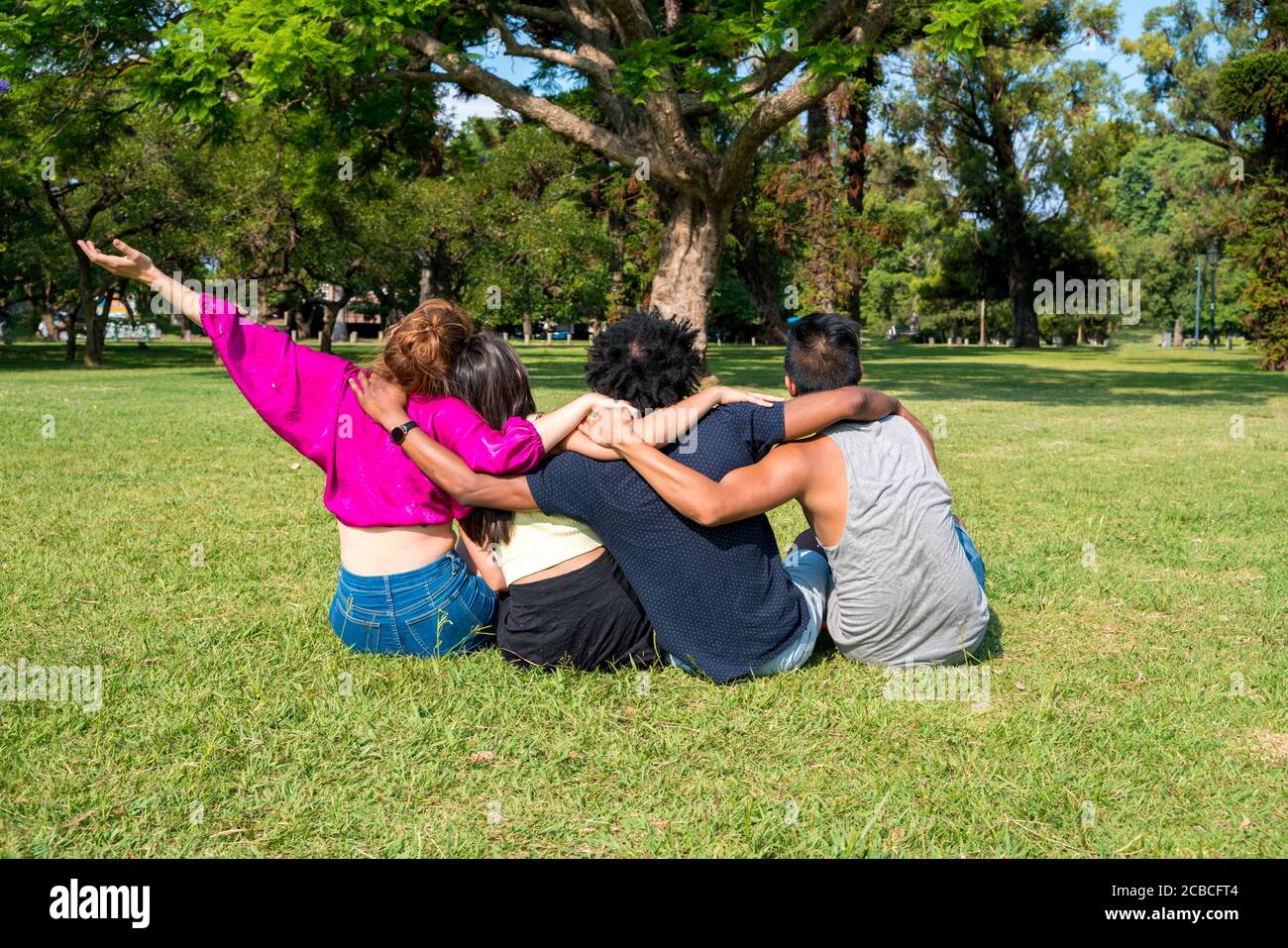 A group of friends sitting together in a park and hugging each other ...
