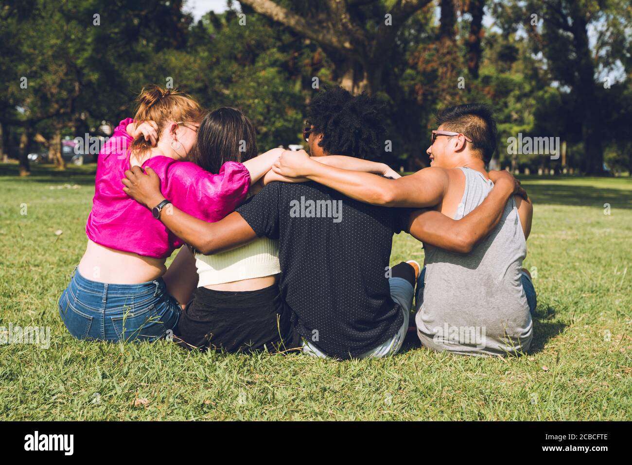 A group of friends sitting together in a park and hugging each other ...