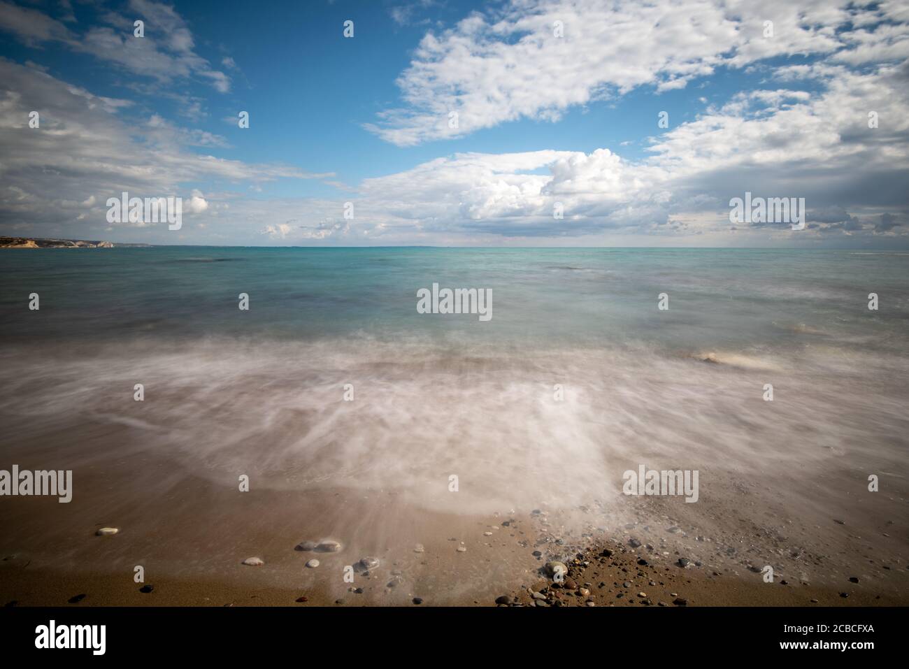Seawaves splashing onto the sandy coast with pebbles and blue cloudy ...