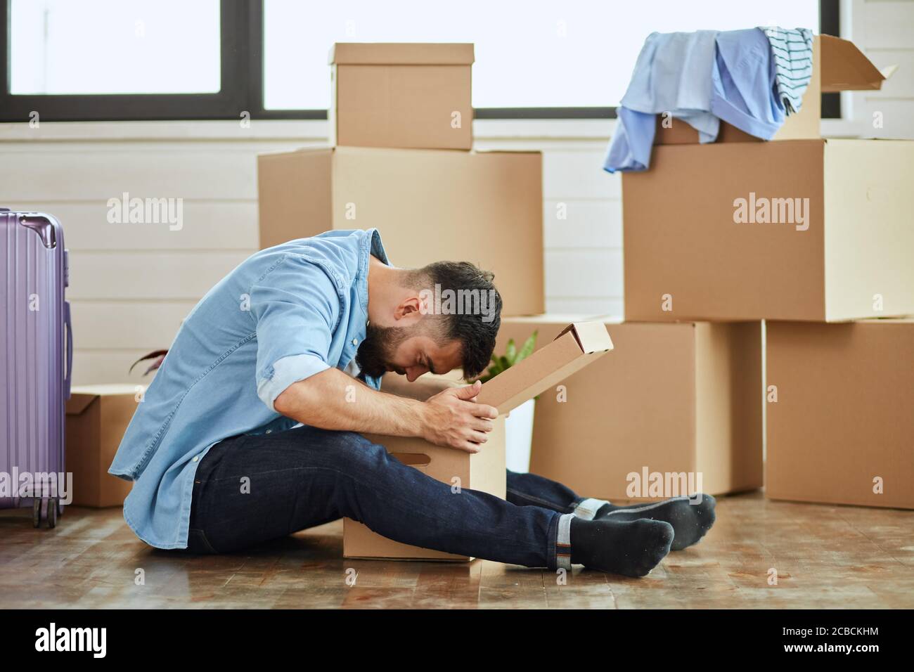 Caucasian man wear blue shirt sit on floor look into box in new house ...