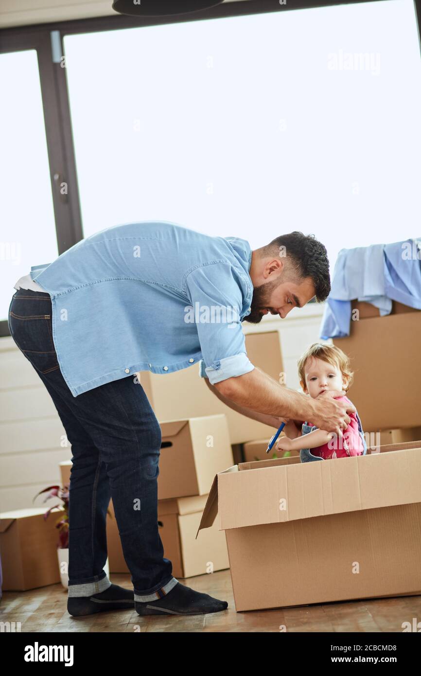 Dad play with daughter sit in moving box. Background moving boxes ...