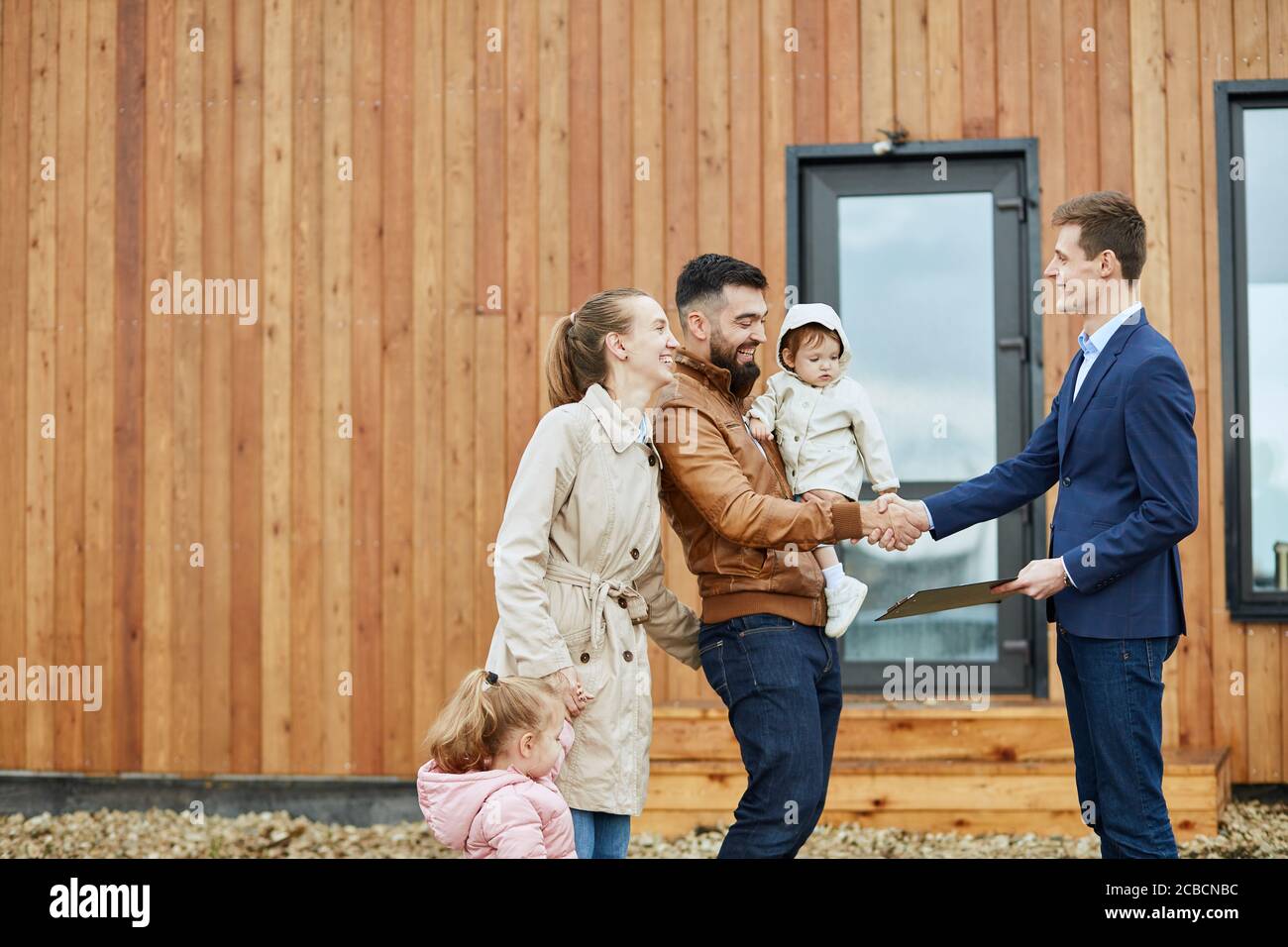 Caucasian happy family of four and realtor wear blue suit stand outdoor ...