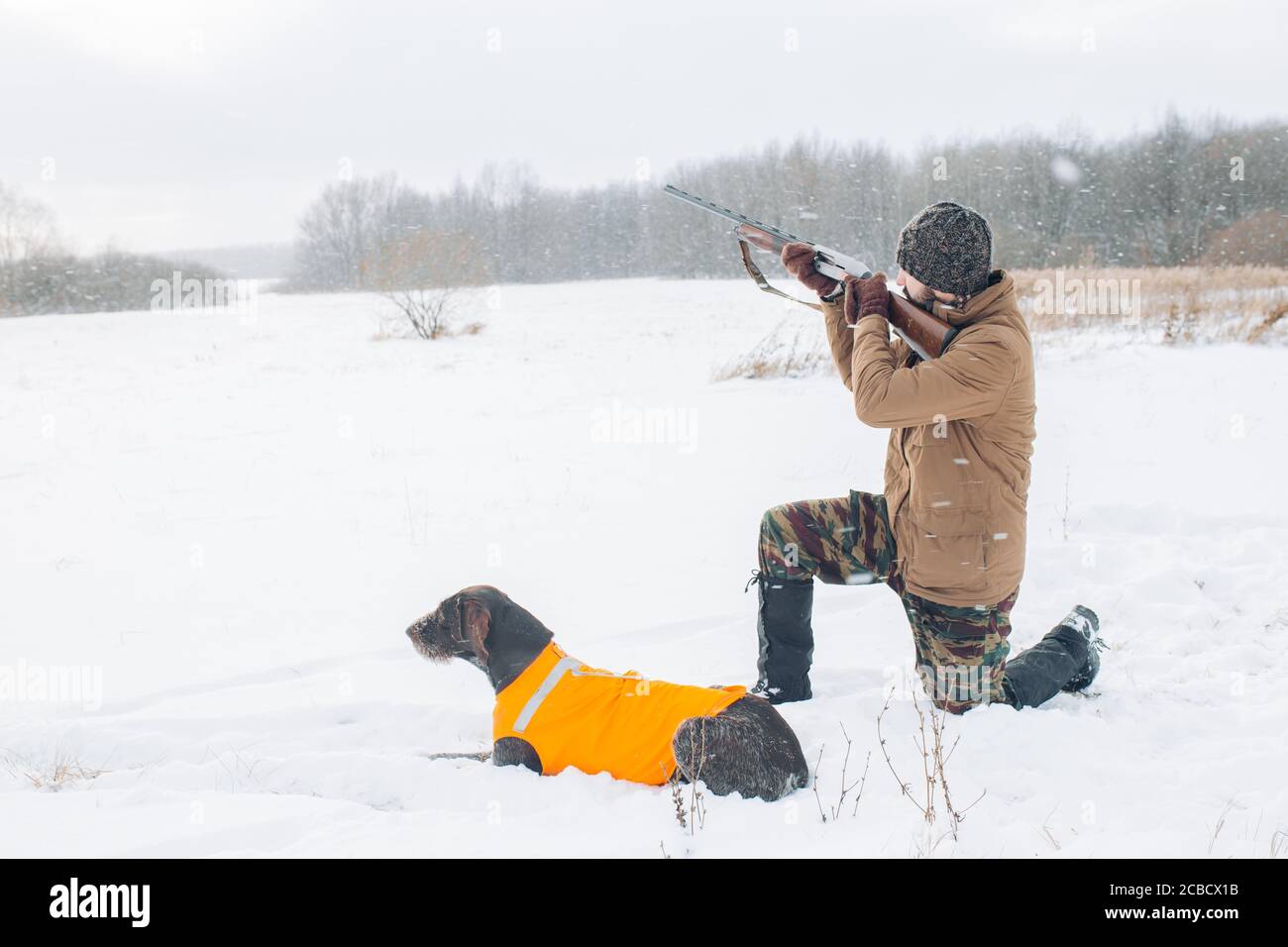 young man is aiming at a bird while dog is waiting for a shot. side ...