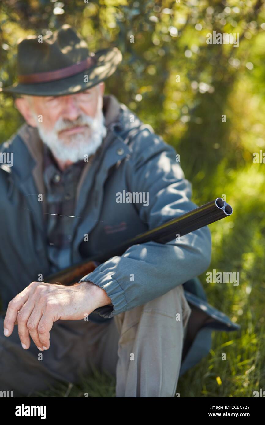 Bearded man with gun sit having rest after good hunting. Forest, grass ...