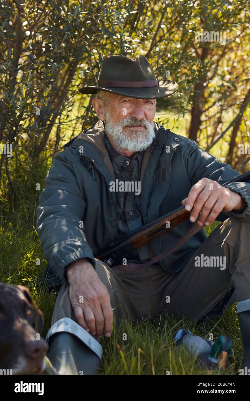Senior hunter with gun sit on grass with dog after hunting Stock Photo ...