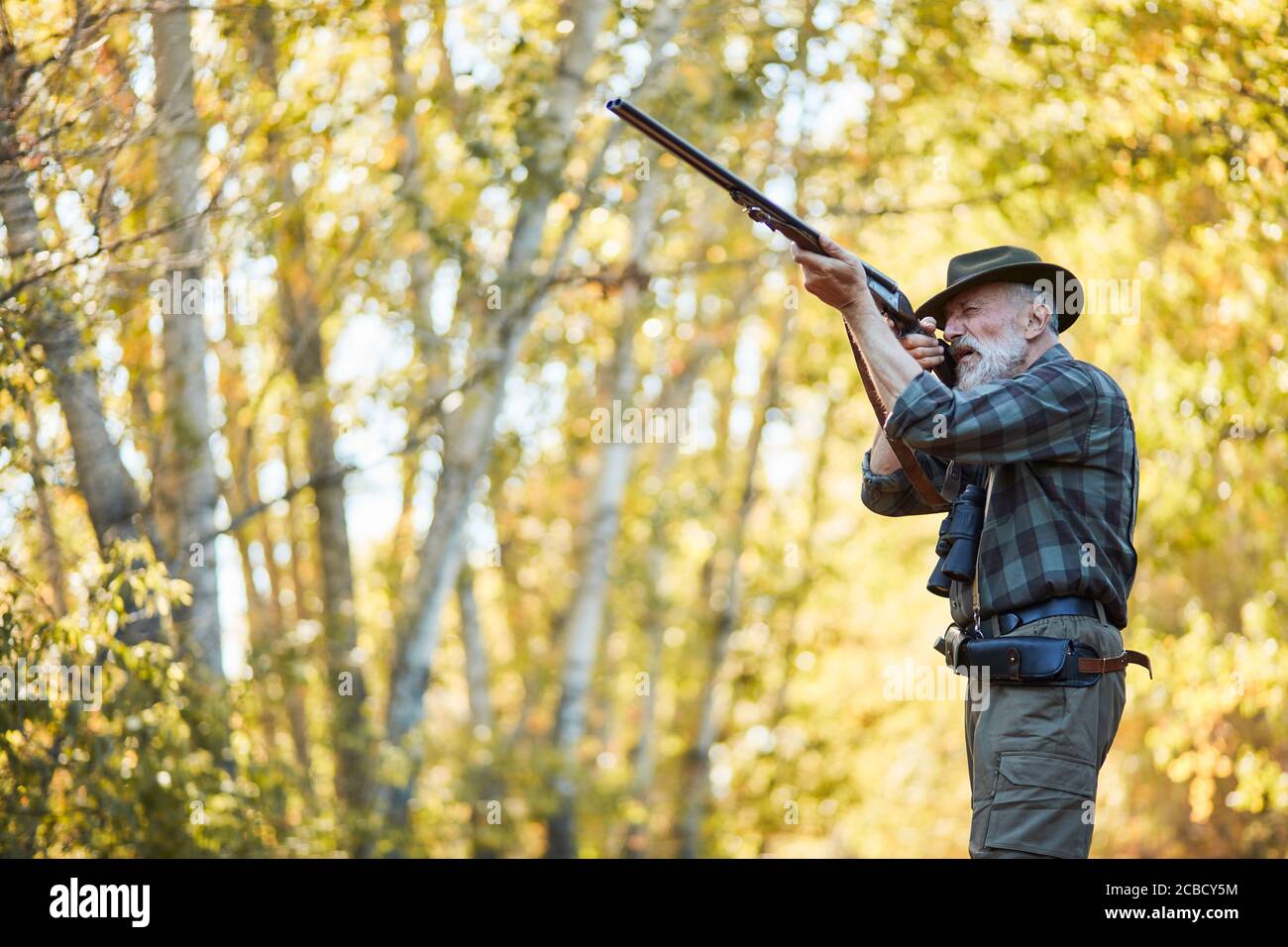 Senior hunter man aims at trophy bird in autumn forest, pointing gun at ...