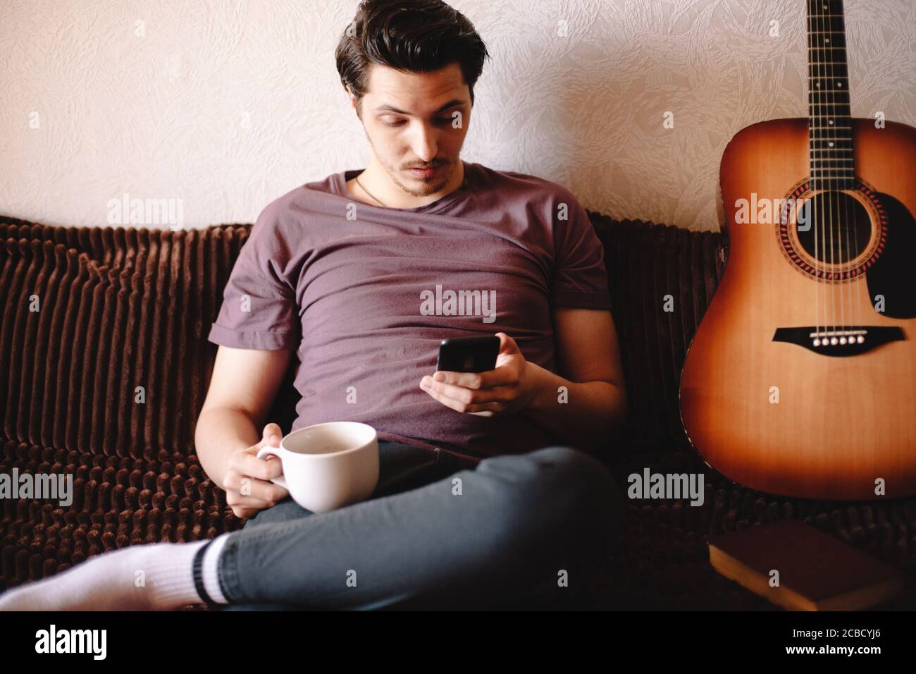 Surprised young man using smart phone while drinking tea at home Stock ...