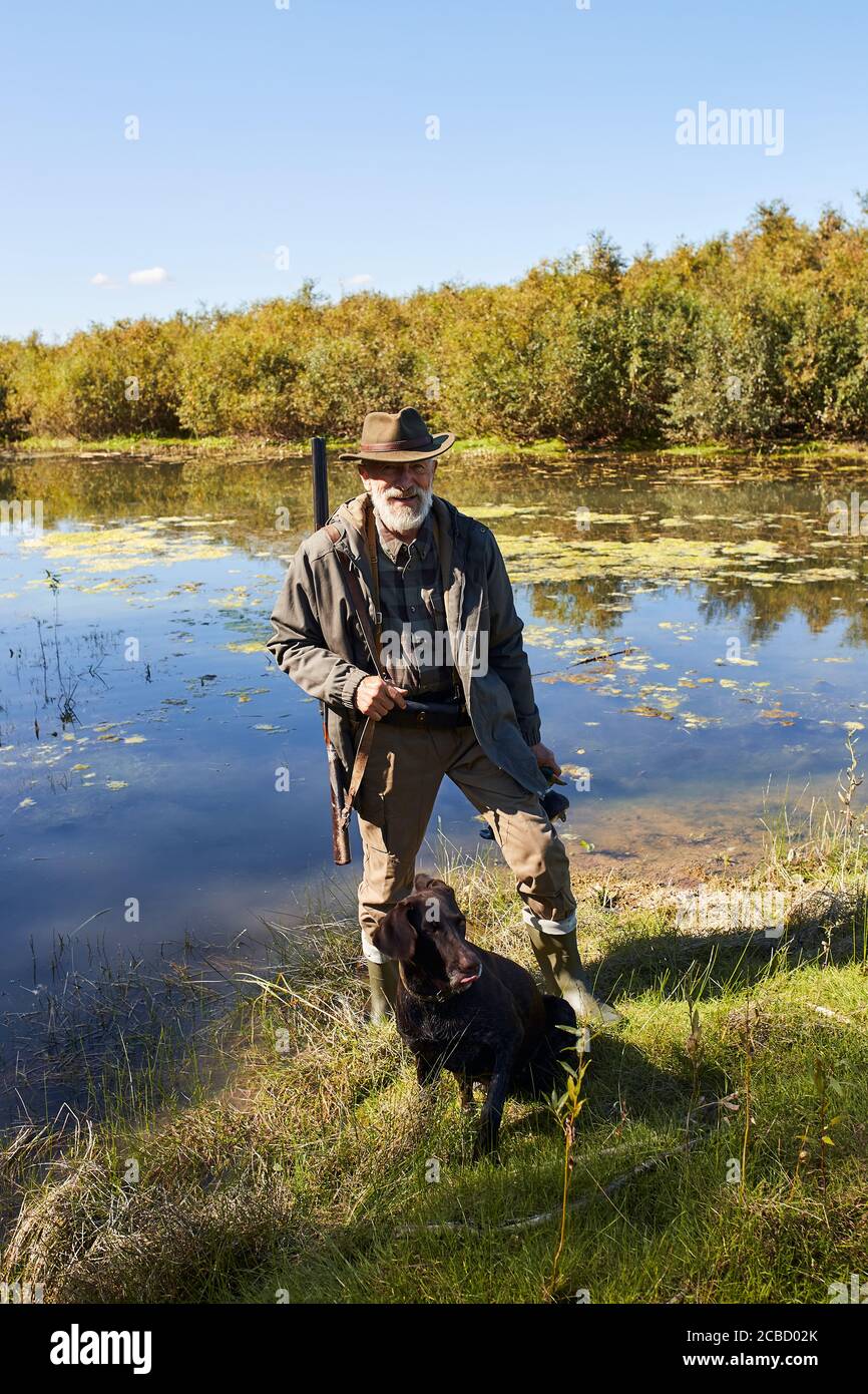 Older hunter man holding trophy duck in hands, hunting with dog on lake ...
