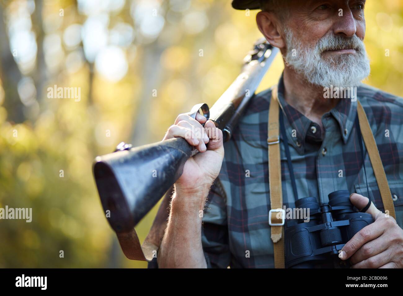 Bearded hunter man with gun on shoulder, binocular in one hand. look ...
