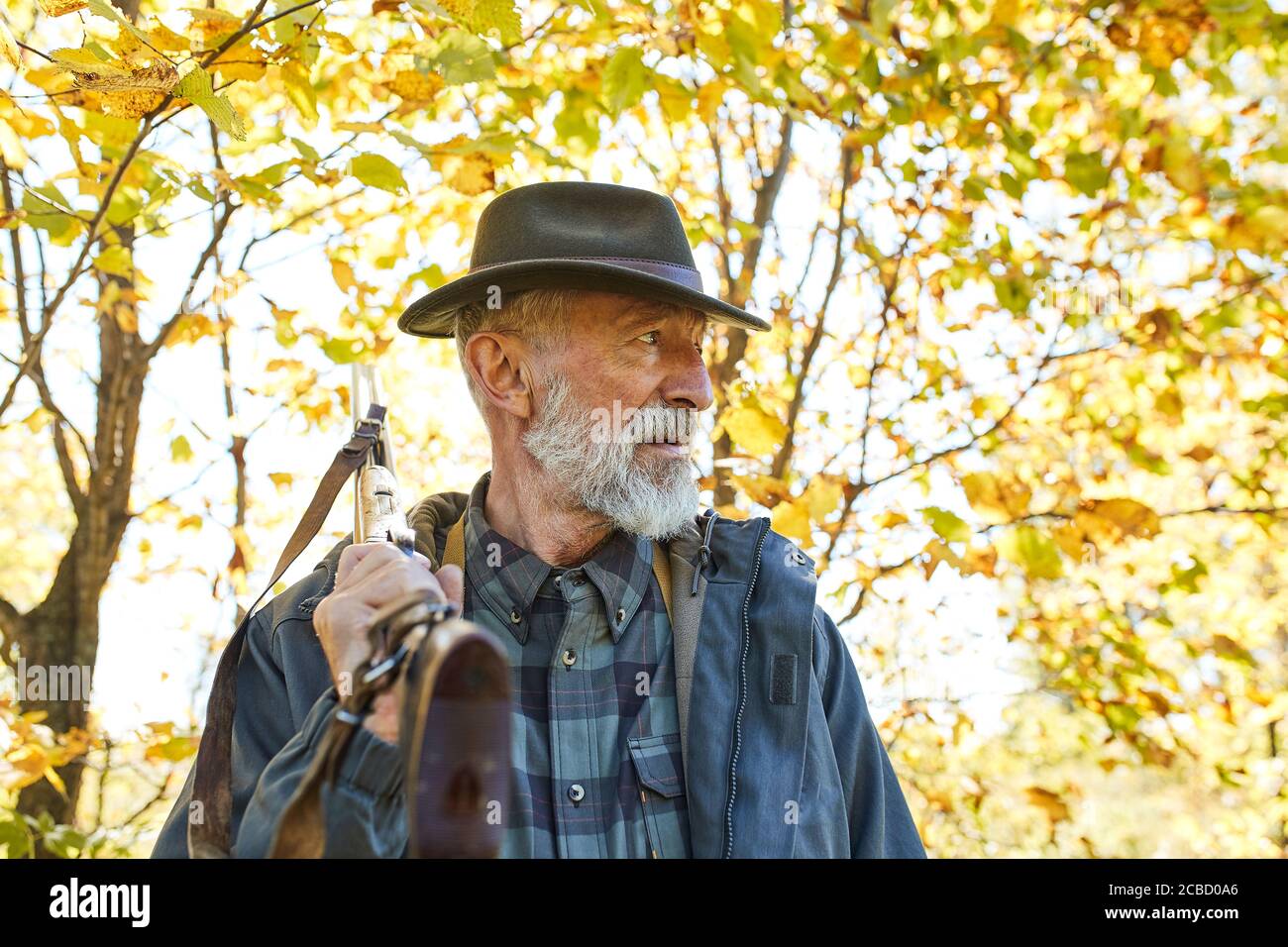 Caucasian senior hunter wearing hat stands with gun on shoulder, looks ...