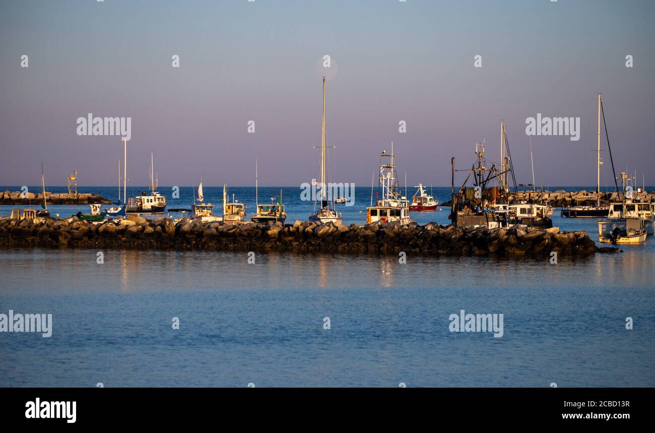 Moon rising above boats and rocks in the ocean Stock Photo - Alamy