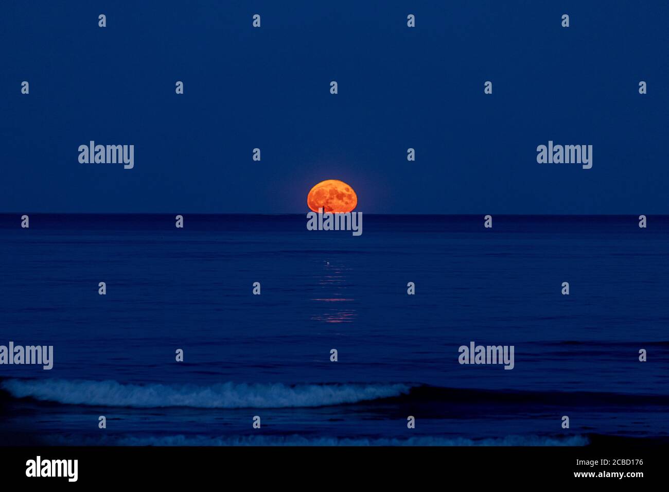 Full moon rising above the ocean horizon with lighthouse in front Stock ...