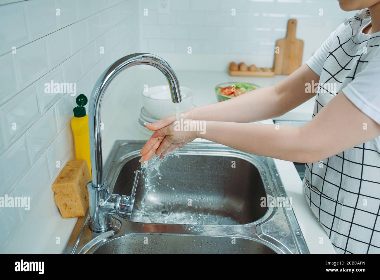 Attractive young woman is washing dishes while doing cleaning at home ...