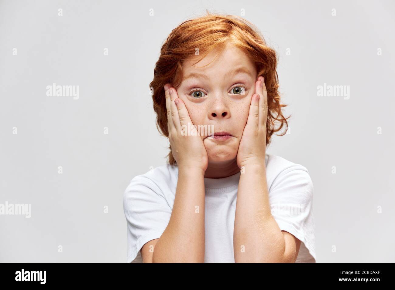 red-haired boy with wide open eyes surprised look hands on face close ...