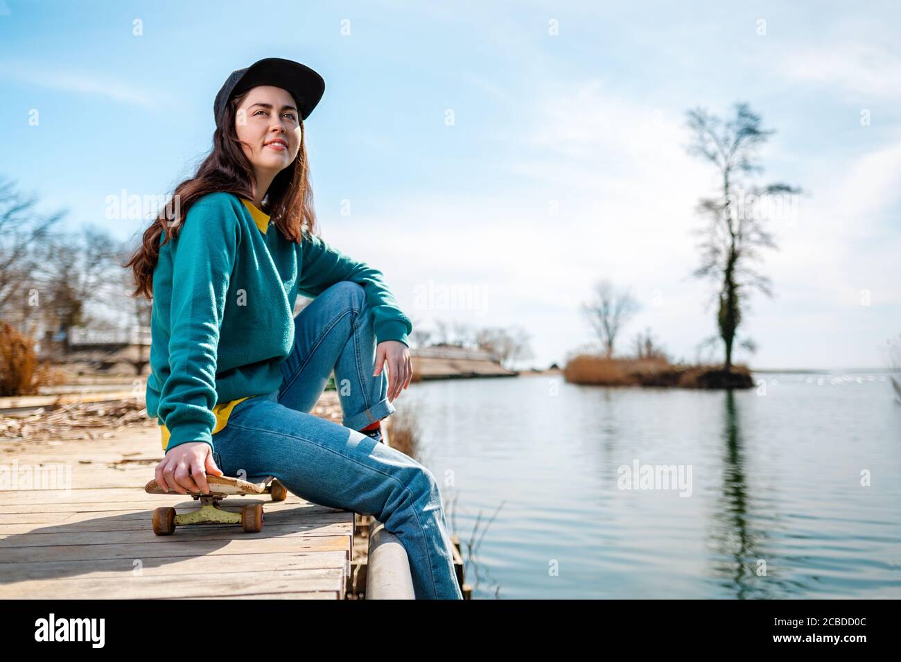 A young Caucasian hipster woman sits on a skateboard with her legs ...