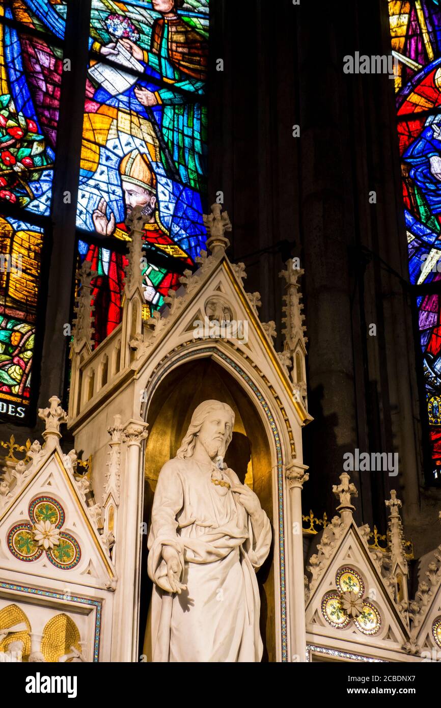 A marble carved statue of Jesus Christ in front of stained glass ...