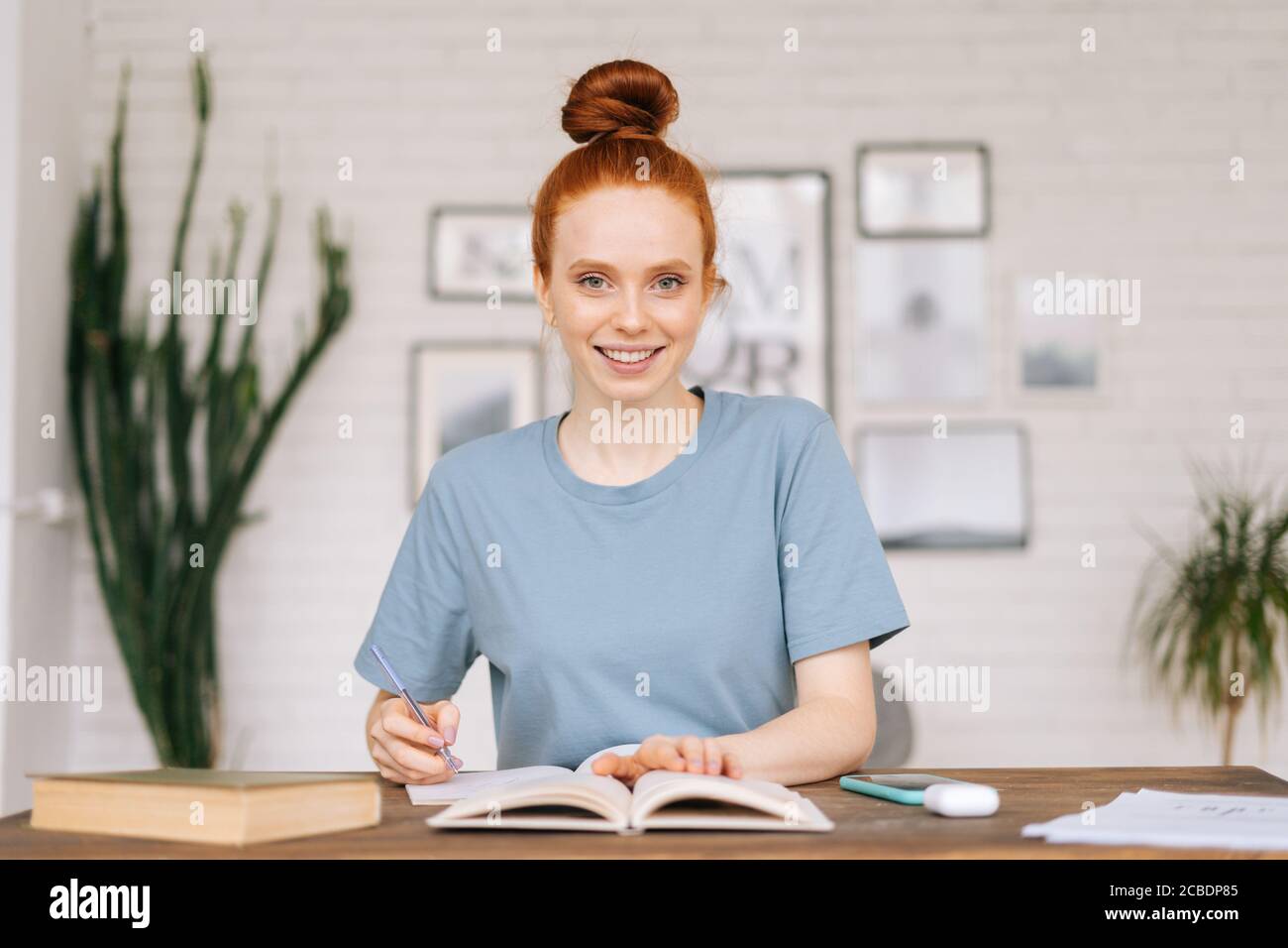 Smiling happy redhead young woman student is making an outline from ...
