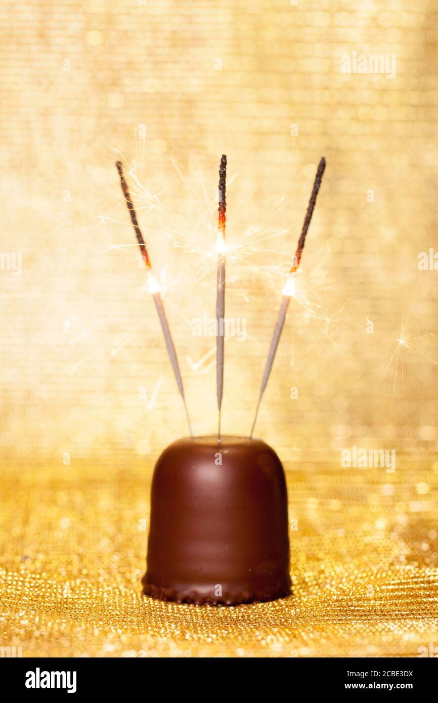 Vertical shot of three sparklers on a chocolate candy with a golden ...