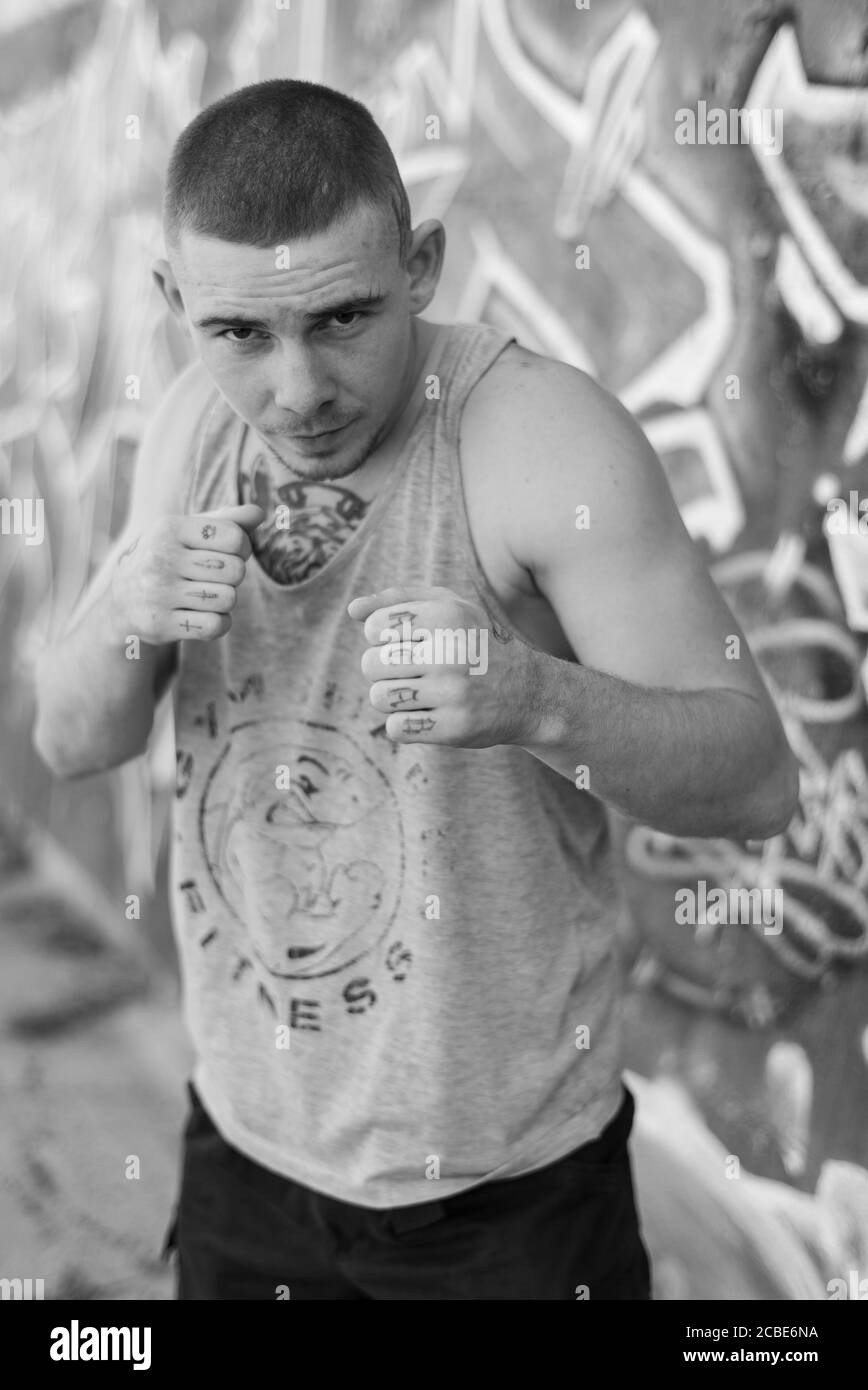 A bully guy in a sports shirt near a wall with graffiti. Black and ...