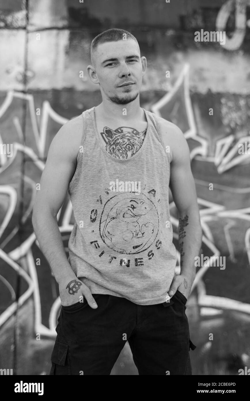 A bully guy in a sports shirt near a wall with graffiti. Black and ...