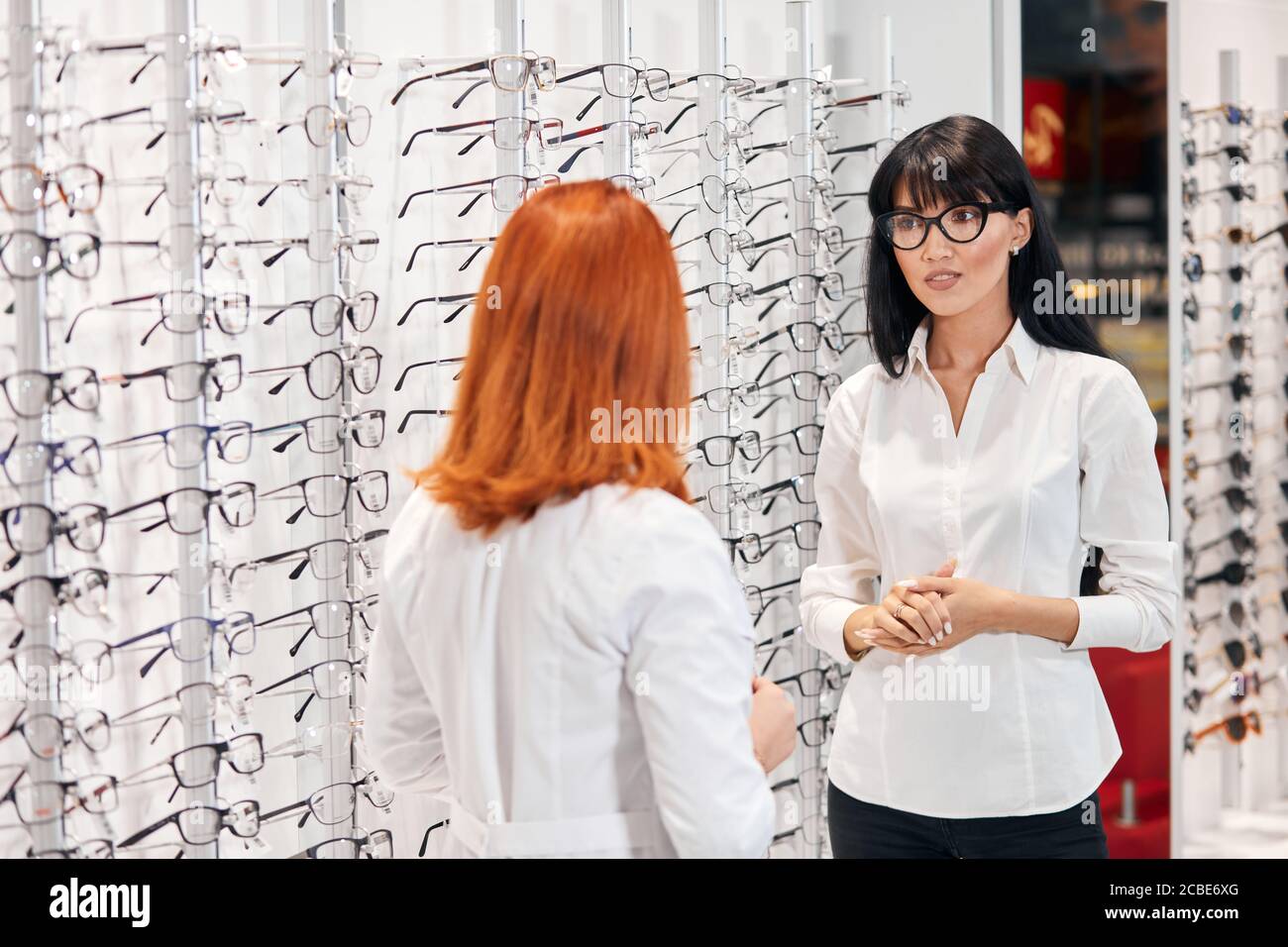 two female beautiful opticians talking about stylish, trendy glasses at ...