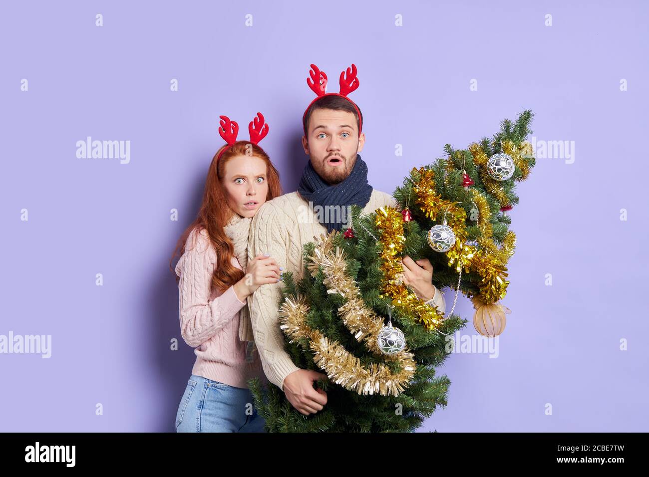 Pretty young couple holding small Christmas tree standing behind ...