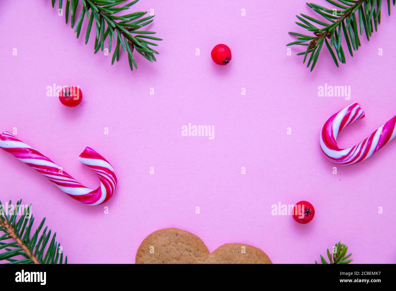 Flat lay shot of candy canes, fir branches, Christmas berries and a heart cookie on a pink ...
