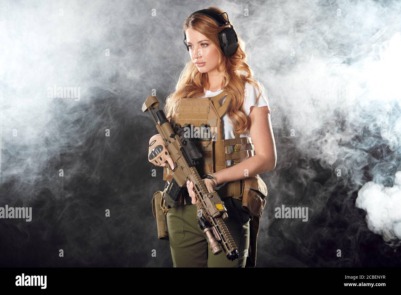 Young blonde female snipper in military outfit with assault rifle in ...